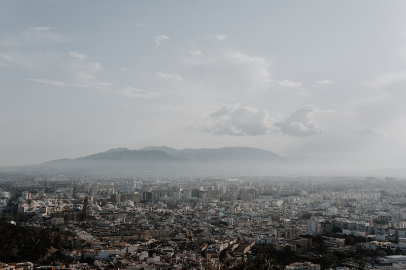 Panoramic view of Malaga city with white buildings cathedral tower and mountain backdrop under clouds