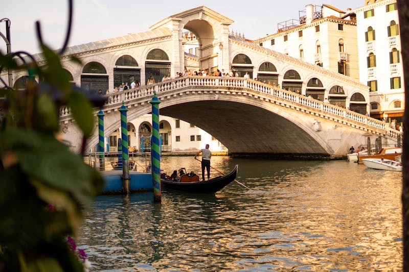 A gondola navigates the Grand Canal with the Rialto Bridge lit by setting sun in Venice