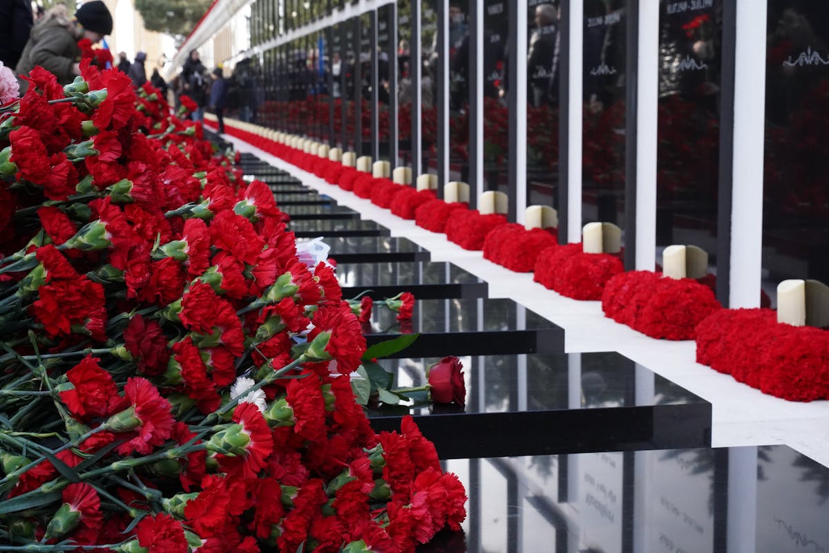 A solemn memorial wall adorned with red carnations and lit candles