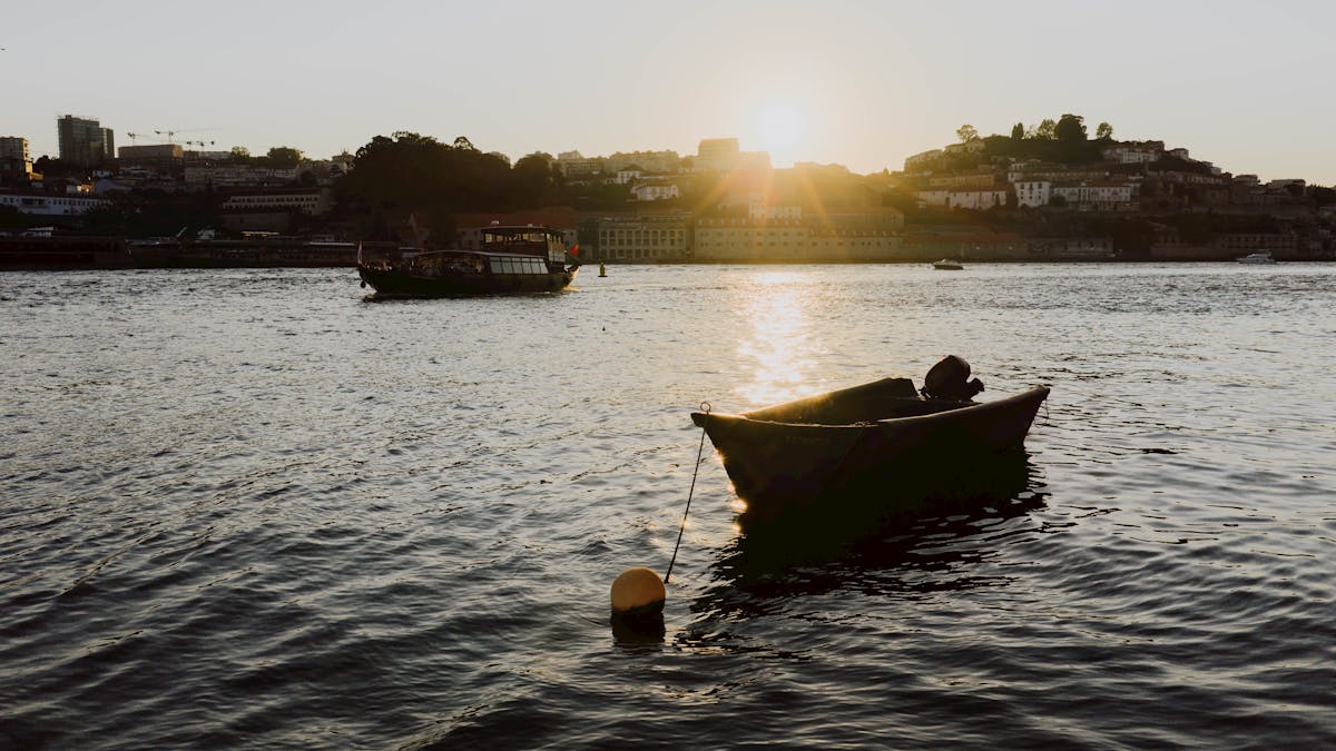 Boats moored on the Douro River with the Porto cityscape silhouetted against a colorful sunset