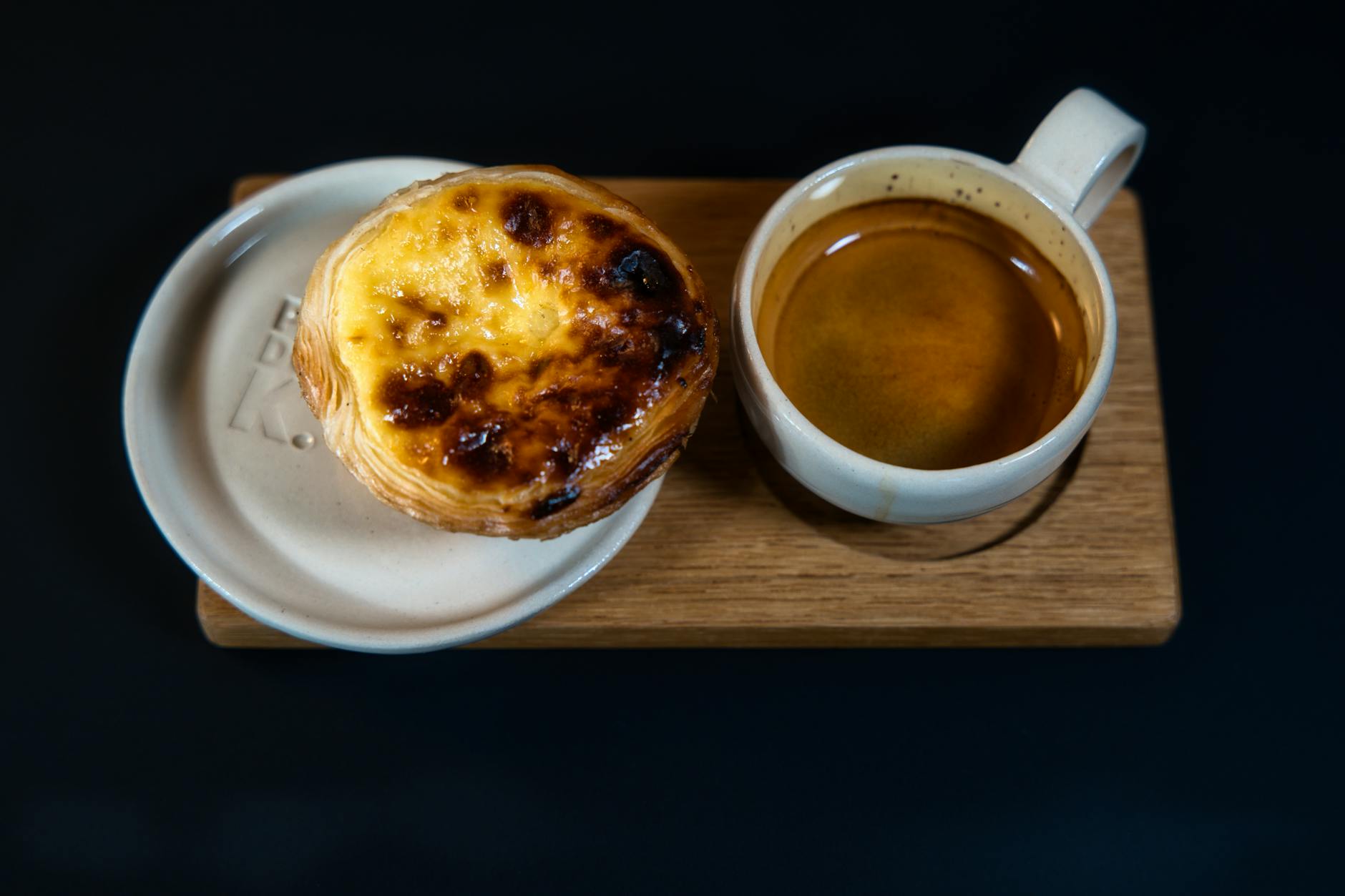 A freshly baked pastel de nata with a cup of espresso on a wooden board