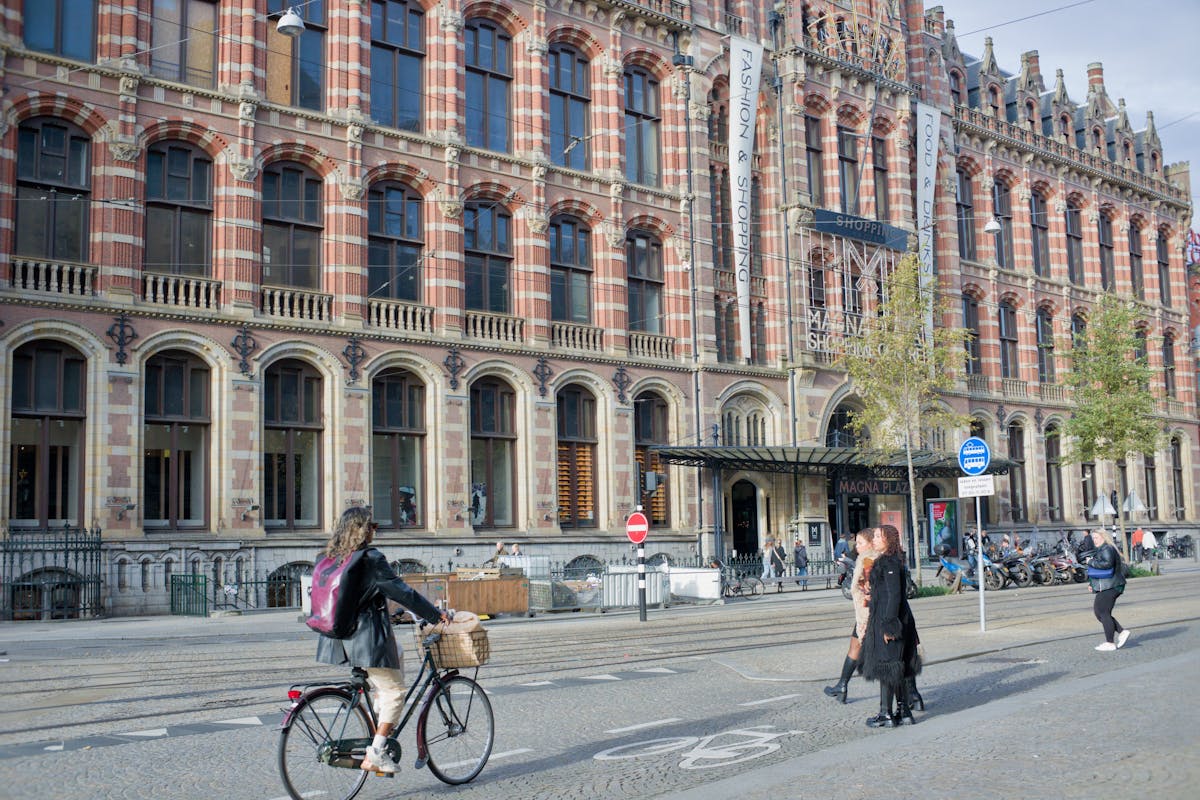 Pedestrians and a cyclist in front of Magna Plaza, a historical Gothic Revival building in Amsterdam