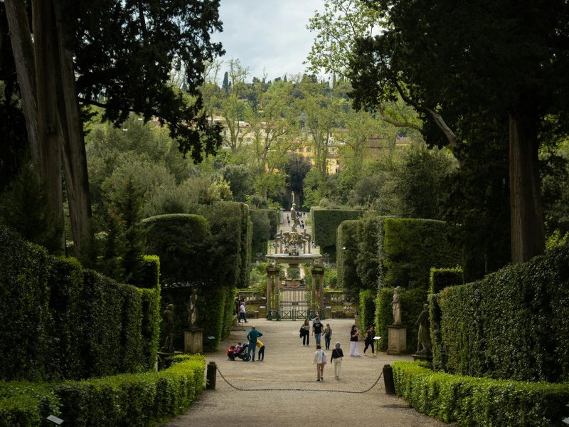 Visitors enjoying a leisurely walk through a garden pathway lined with classical statues and greenery