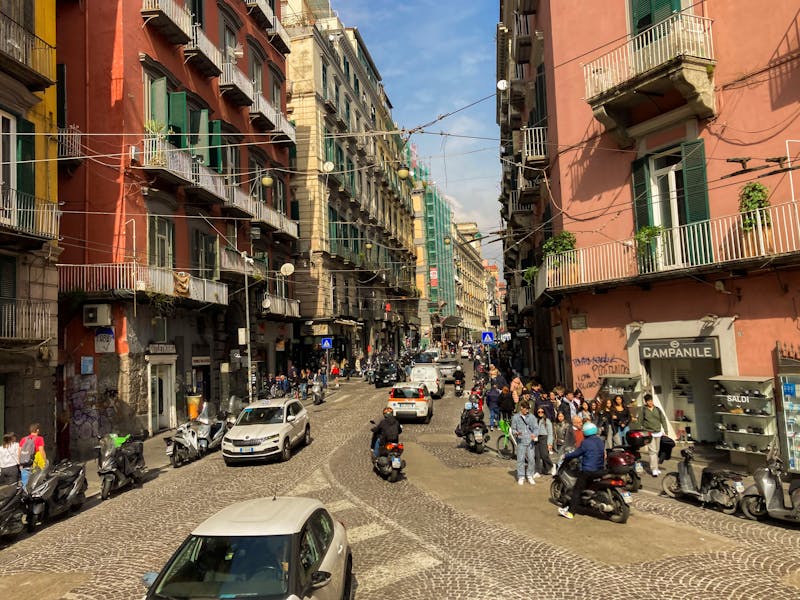 A street in Naples Italy with scooters, pedestrians, and historic buildings on a sunny day