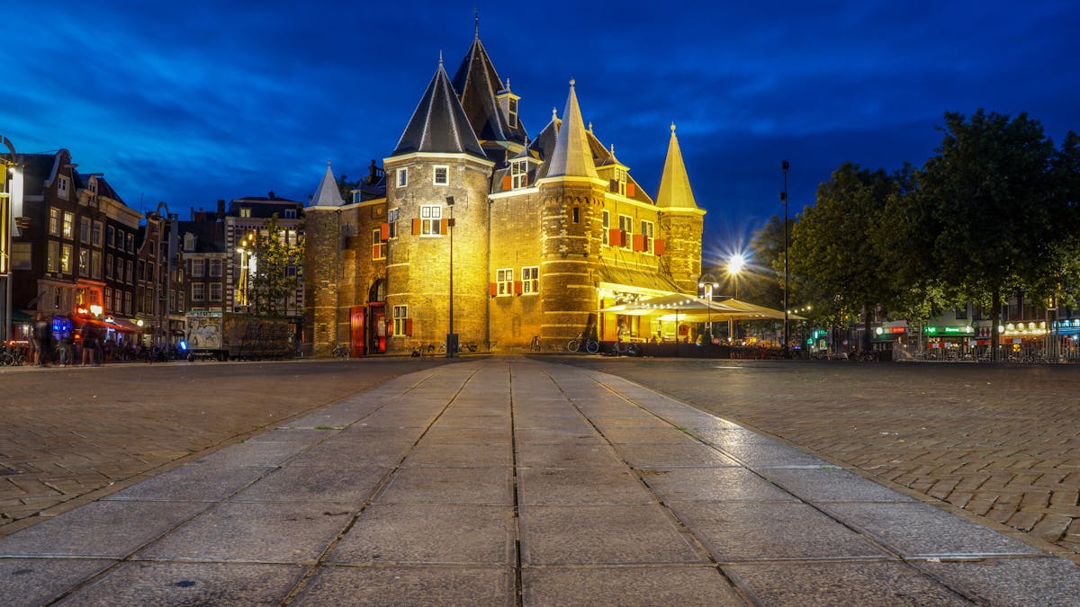 A grand historic building in Amsterdam illuminated at night, with warm lighting against the dark sky