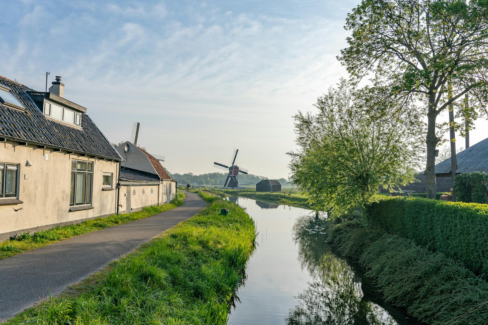 Serene Dutch countryside view with canal, houses, and windmill on a sunny day