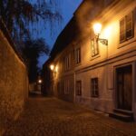 Narrow cobblestone street in Prague Old Town lit by warm lantern light at night