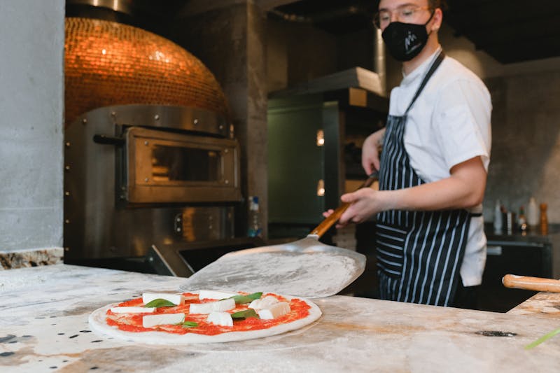 Chef preparing a Neapolitan pizza in a rustic kitchen with a wood-fired oven