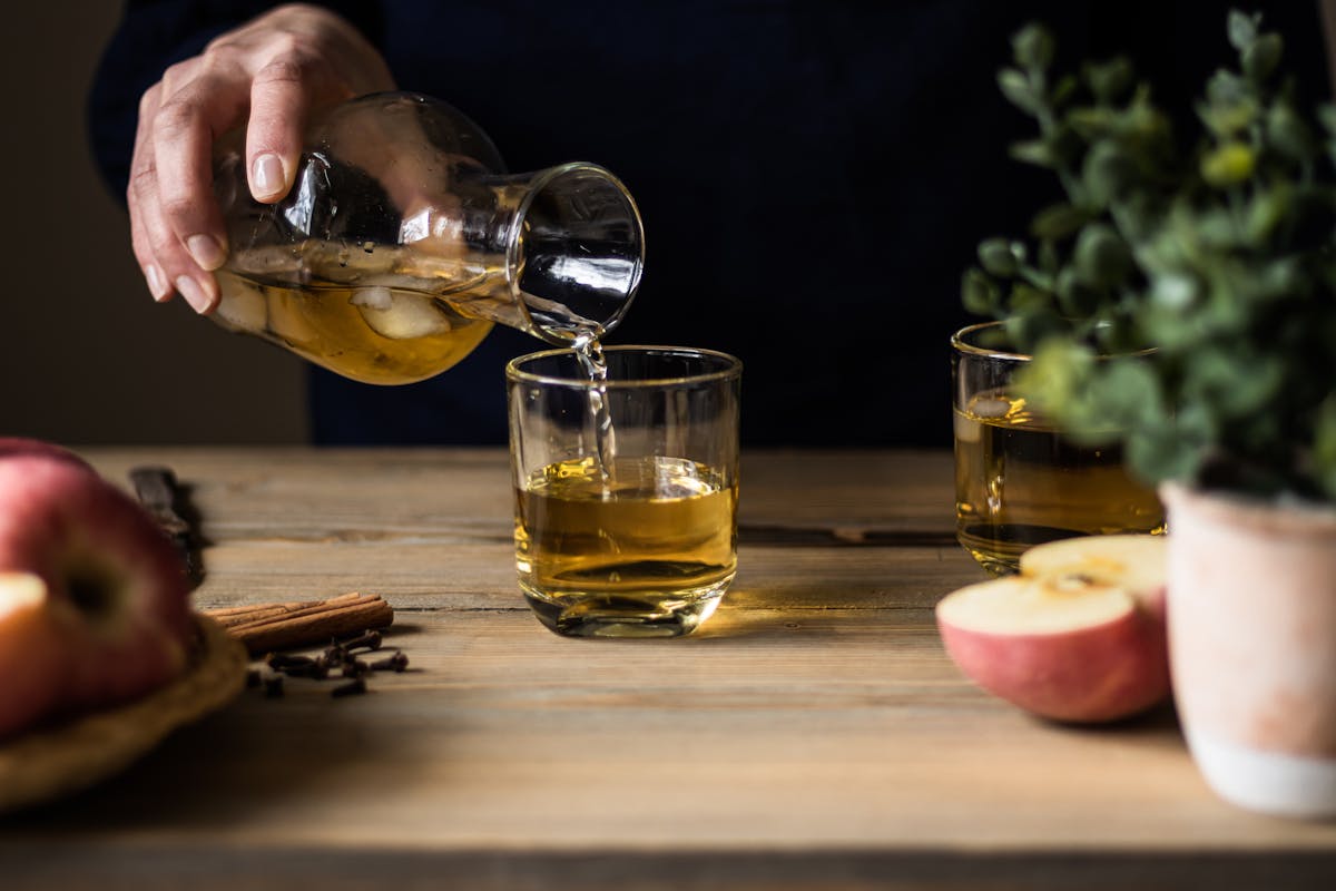Apple cider being poured into glasses on a wooden table with fresh apples