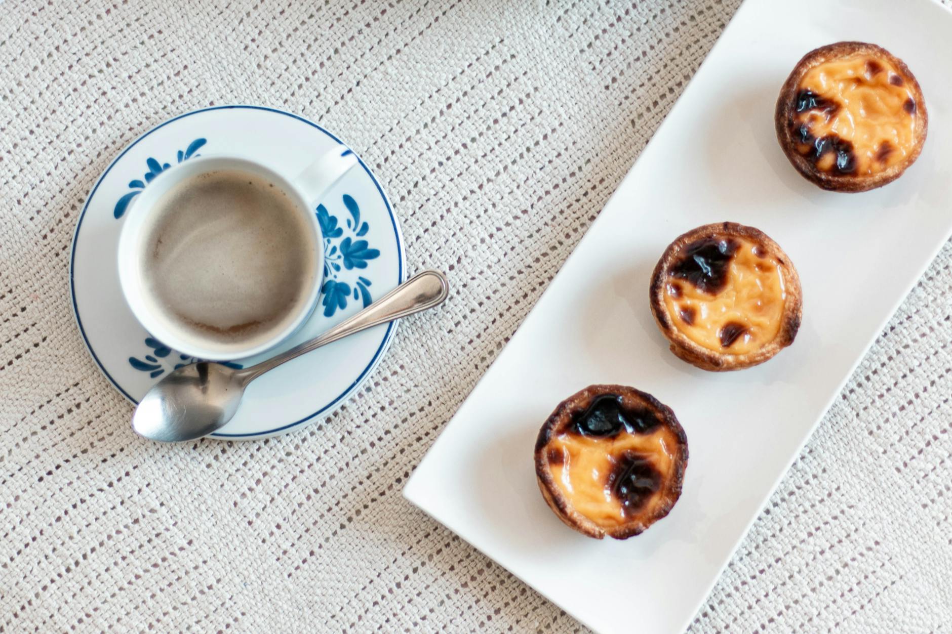 Cup of coffee with three golden custard tarts on a decorative lace tablecloth