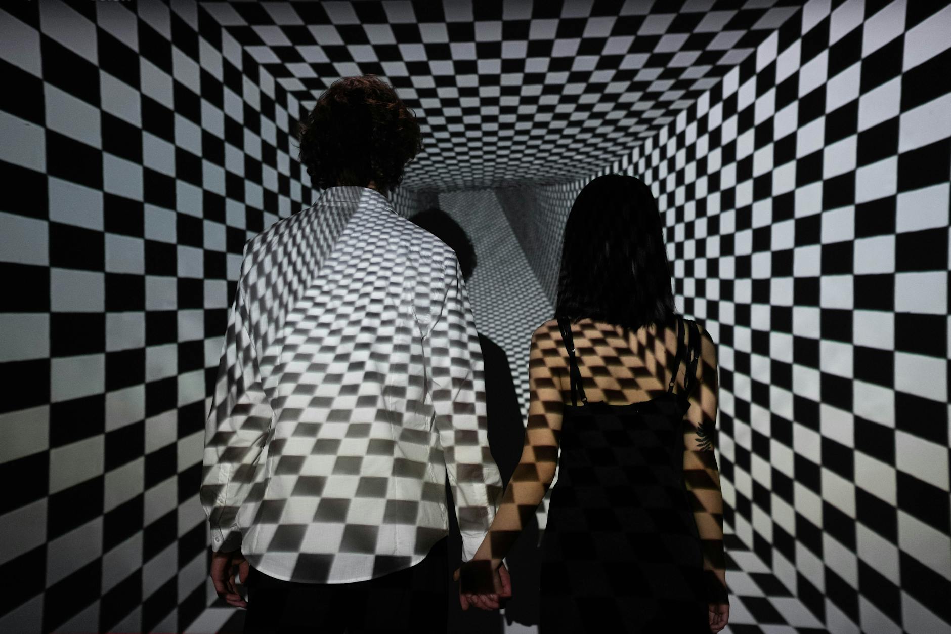 A couple walking through a black and white checkerboard tunnel creating an optical illusion effect