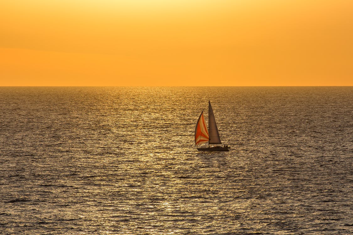Beautiful sunset with a sailboat sailing across the golden ocean horizon