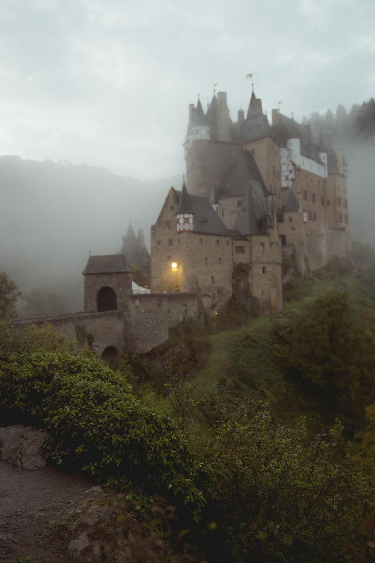Eltz Castle shrouded in morning fog among lush greenery