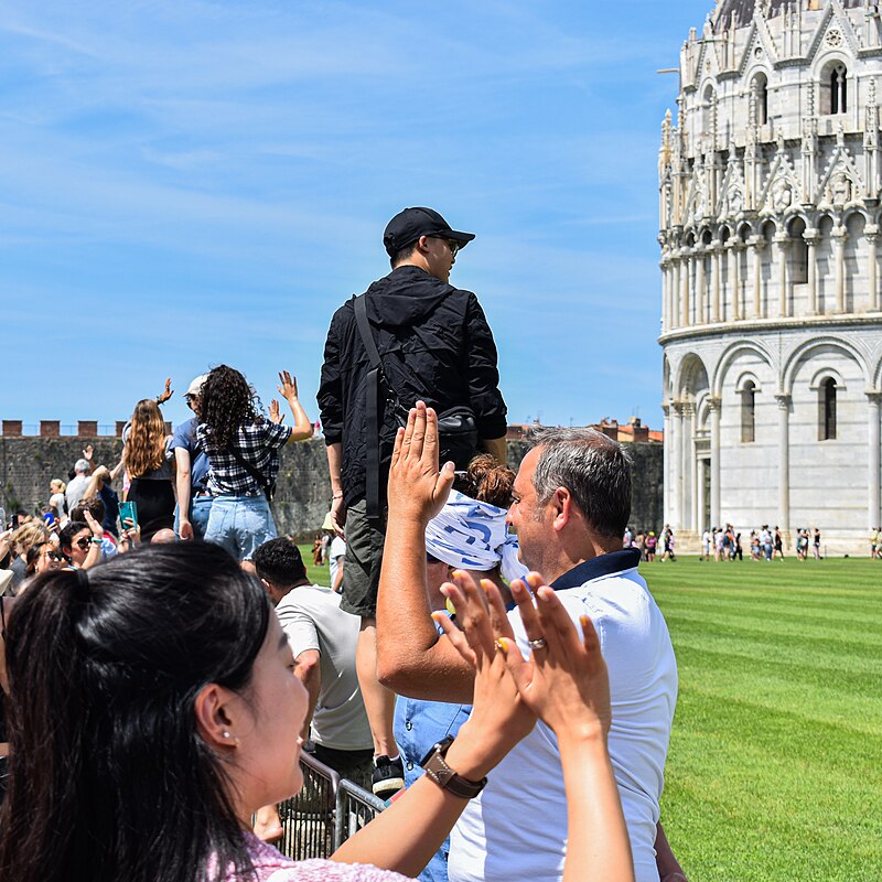 Tourists on the lawn posing to hold up the Leaning Tower of Pisa