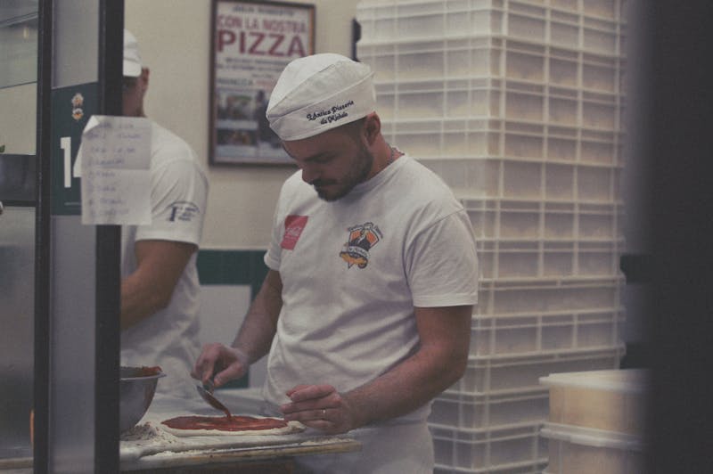 Pizza chef spreading sauce on pizza dough in a Naples restaurant kitchen