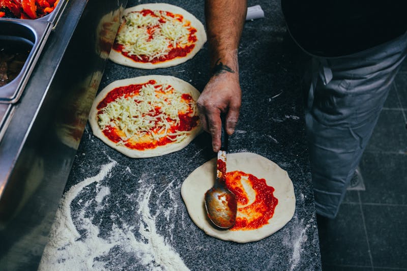 Chef spreading tomato sauce on pizza dough in a professional kitchen