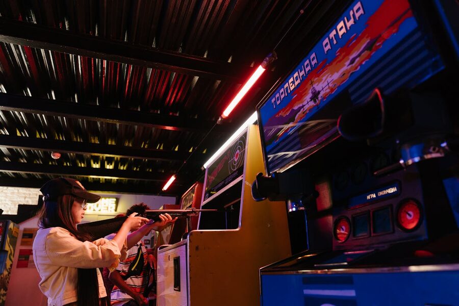 Teenage girl enjoying a retro shooting game at an indoor arcade with colorful neon lights