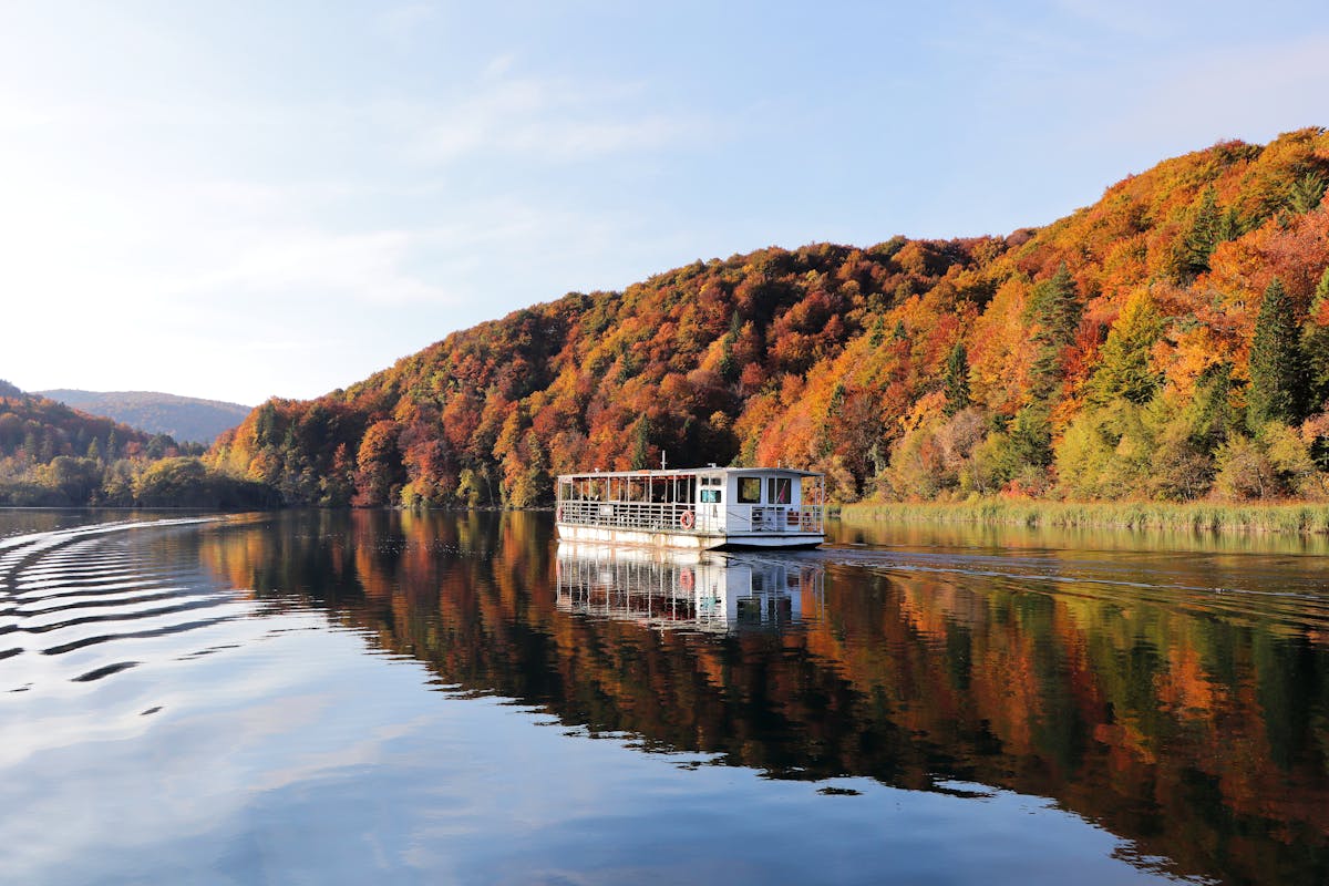 Boat cruising on lake with autumn foliage reflections at Plitvice Lakes Croatia