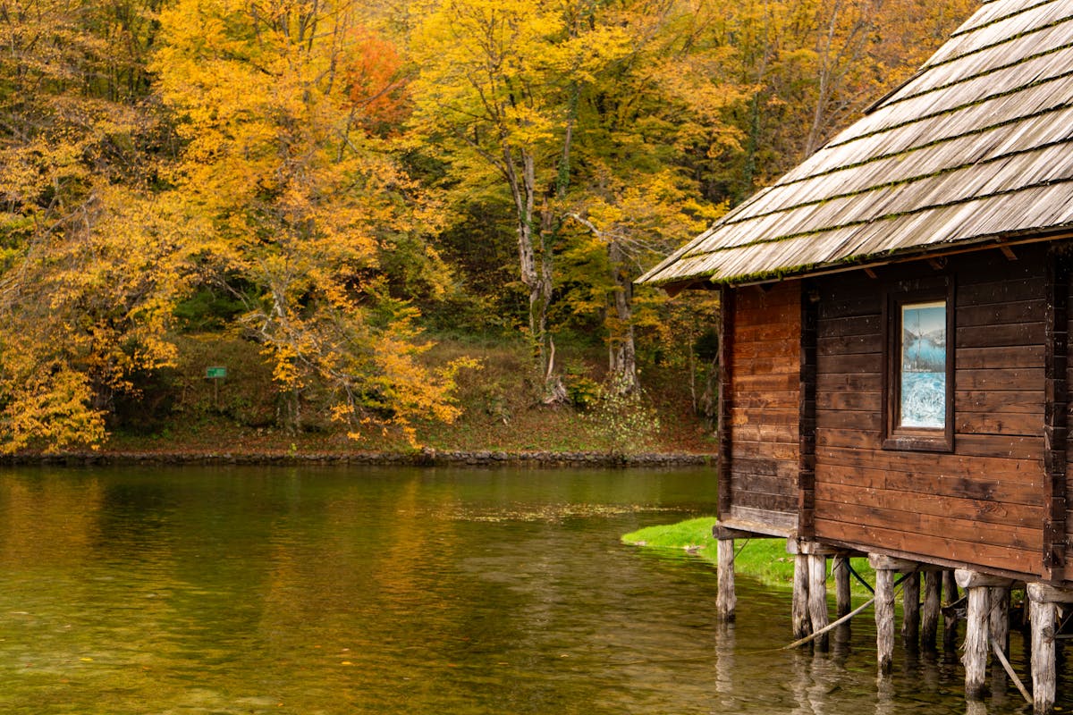 Wooden hut by a reflective lake surrounded by autumn foliage at Plitvice Lakes