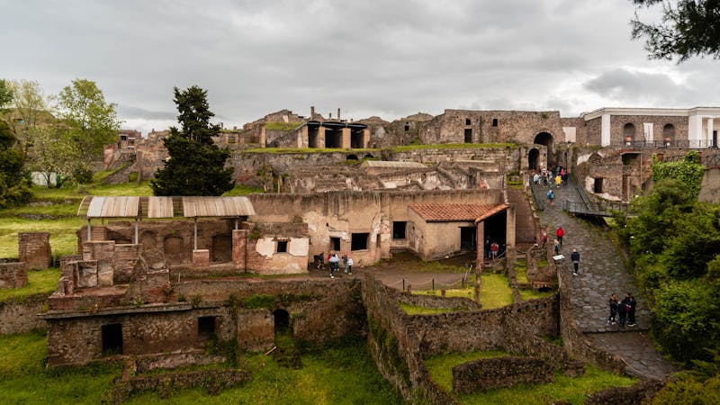The Suburban Baths building in Pompeii with restored walls and greenery under cloudy skies