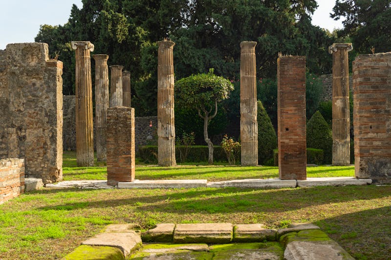 Historic columns surrounding a garden area in Pompeii with greenery growing between the ancient stonework