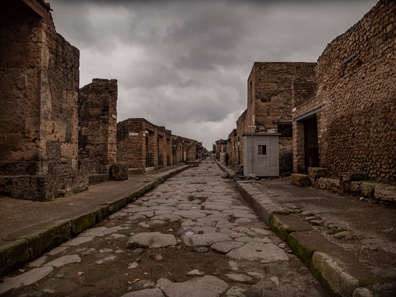 A deserted ancient street in Pompeii with stone ruins on both sides under overcast sky