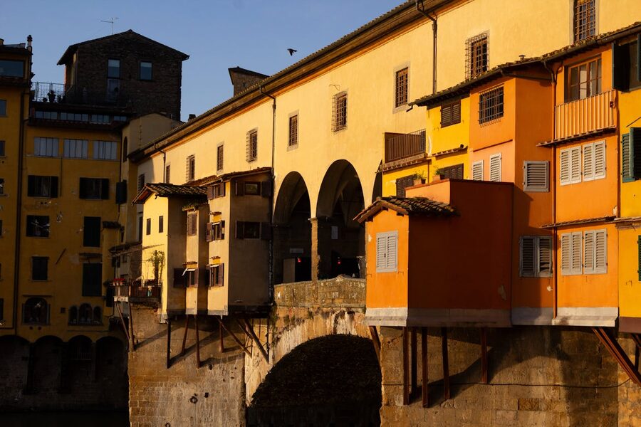 Warm golden hour light illuminating the colorful buildings along Ponte Vecchio in Florence