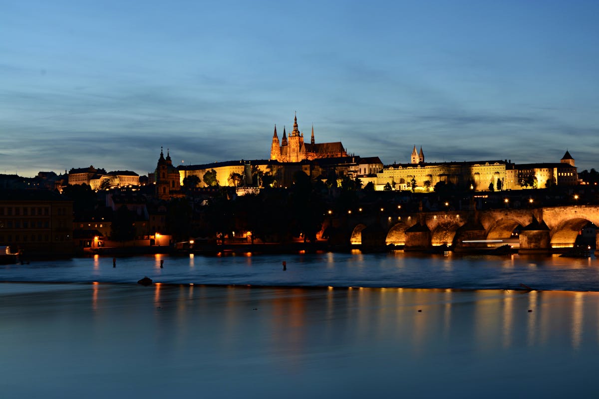 Prague Castle illuminated at dusk with Charles Bridge visible across the Vltava River