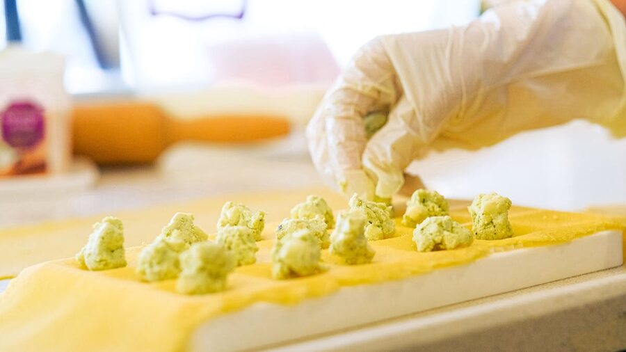 Hands preparing ravioli with ricotta filling on a pasta sheet