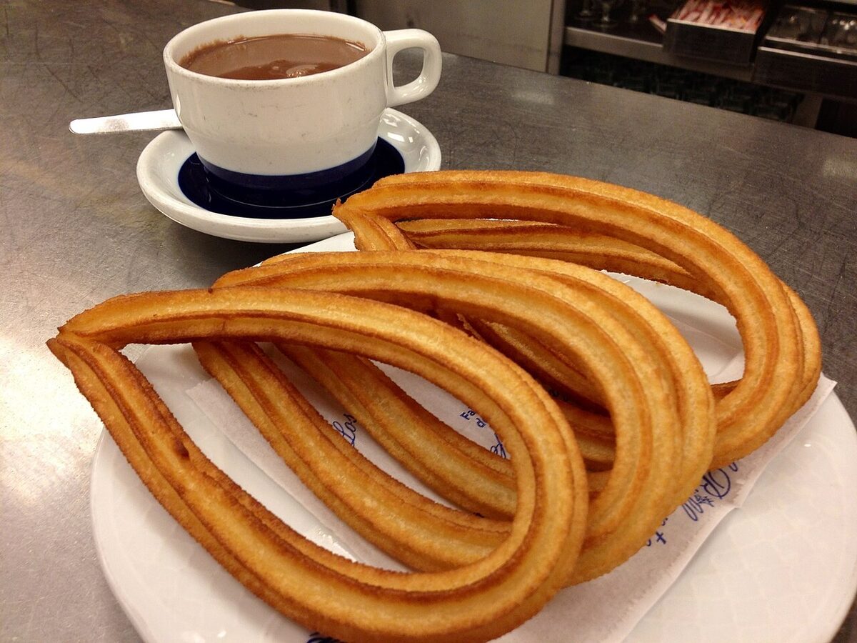 Plate of golden churros with thick Spanish hot chocolate for dipping