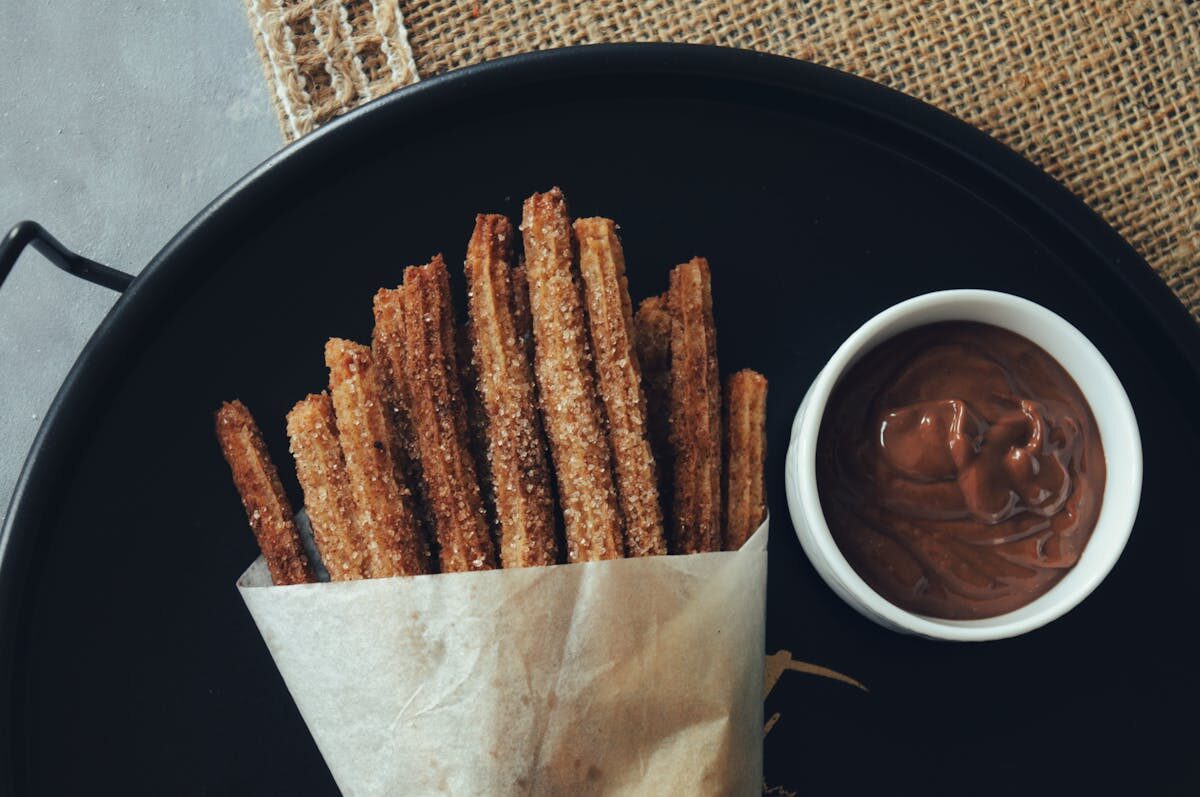 Tray of fresh churros wrapped in paper with a bowl of rich chocolate dipping sauce