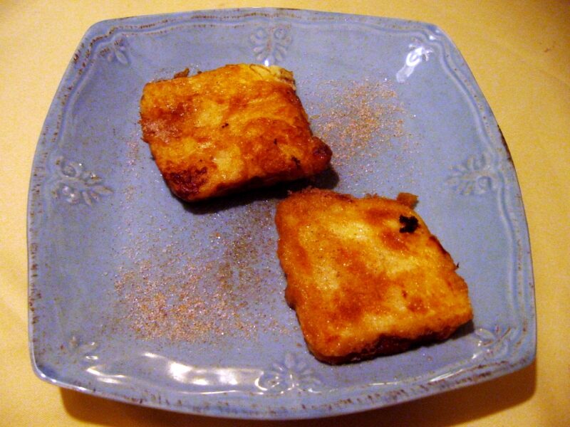 Golden fried leche frita pieces dusted with cinnamon sugar on a serving plate