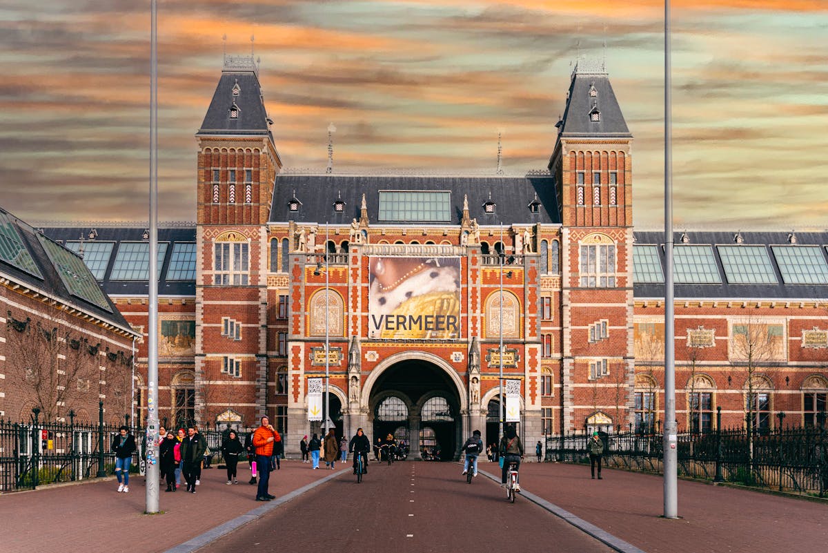 Visitors walking past the iconic Rijksmuseum entrance in Amsterdam during sunset