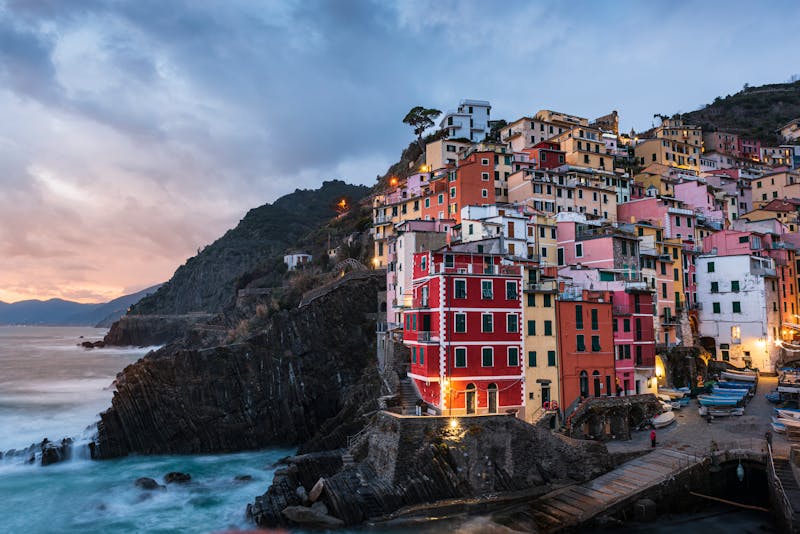 The colorful cliffside village of Riomaggiore illuminated at dusk with houses cascading down toward the Ligurian Sea