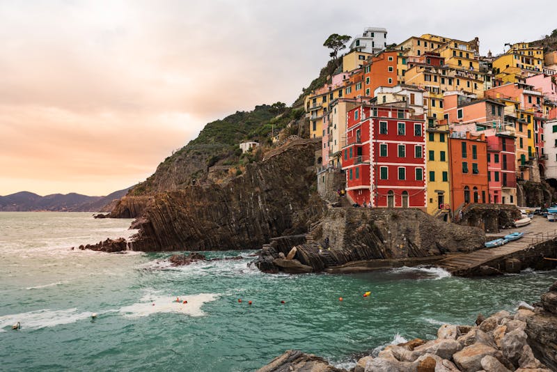 Brightly painted houses clinging to the steep cliffs of Riomaggiore overlooking the calm waters of the Ligurian Sea