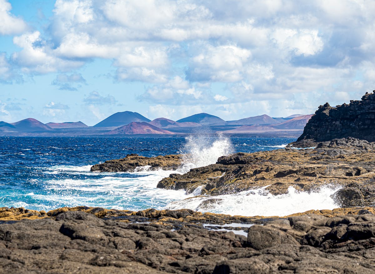 Waves crashing against a rugged rocky coastline under a bright sky