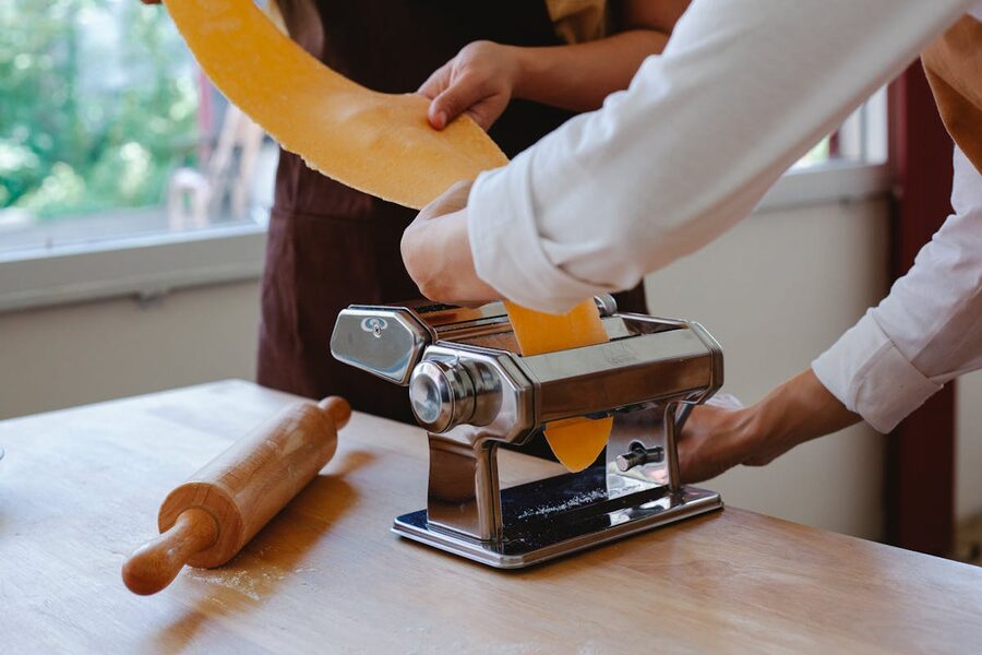 Hands feeding pasta dough through a traditional hand-cranked pasta maker