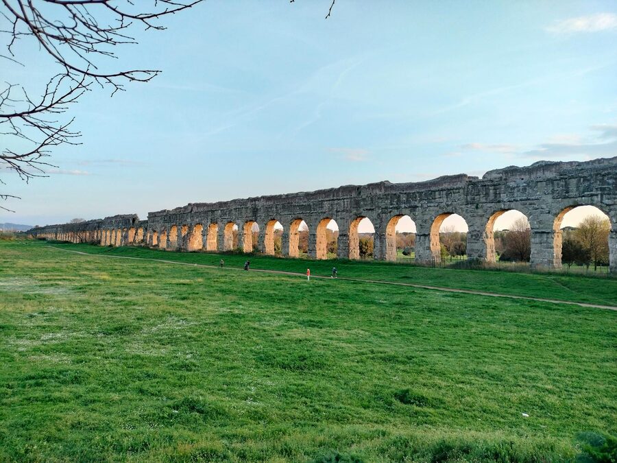 View of an ancient Roman aqueduct in a lush green park at sunset in Rome