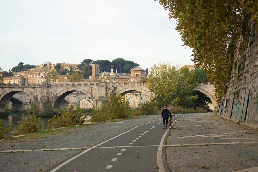 A cyclist walks along a path by a historic bridge in Rome Italy