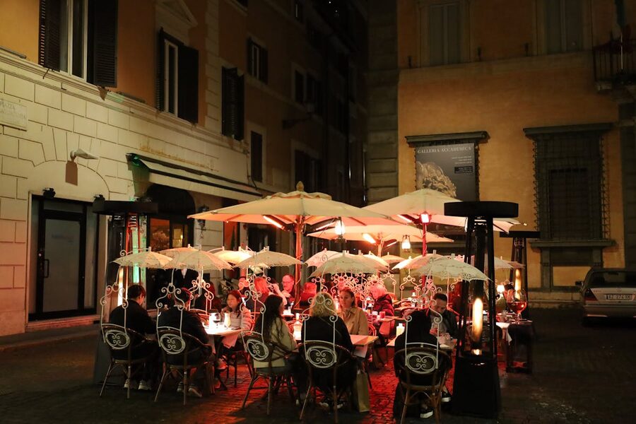 Outdoor dining scene in Rome at evening with warm lighting and umbrellas