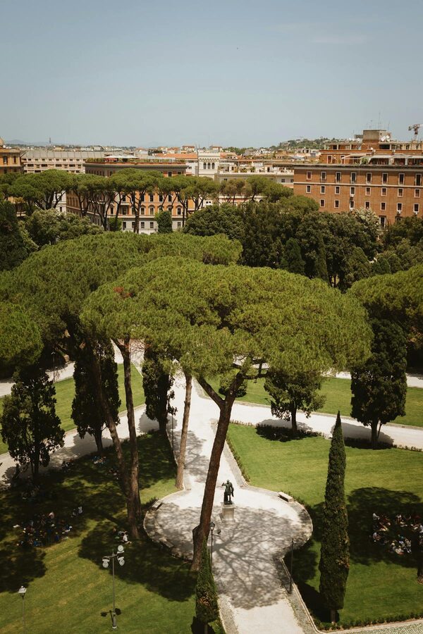 A scenic path through lush green gardens in Rome with mature trees and sunlight