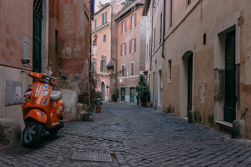 An orange scooter parked on a cobblestone street in Trastevere Rome