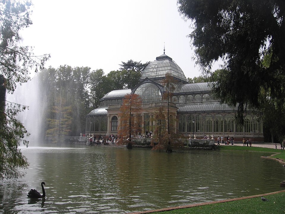 The Crystal Palace glass structure in Retiro Park Madrid surrounded by trees and reflected in water