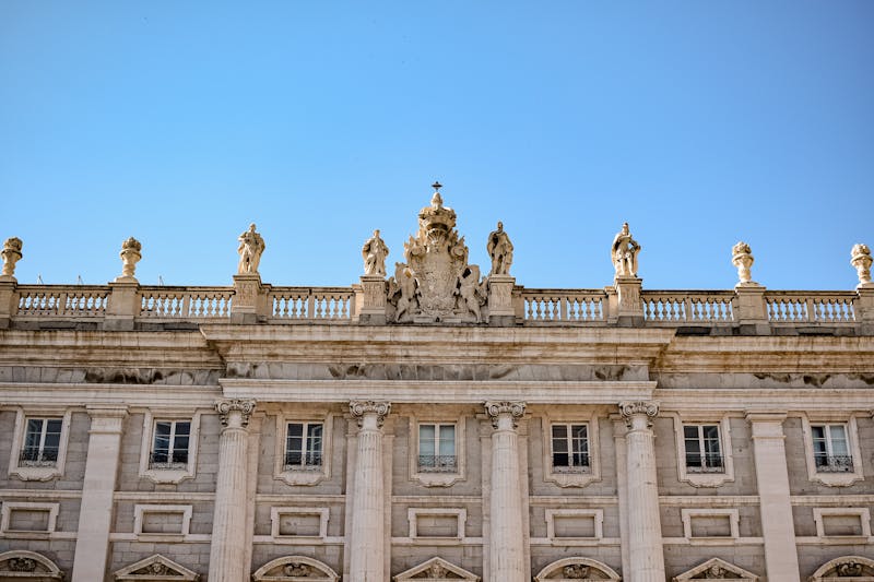 Detailed view of ornate sculptures atop the Royal Palace in Madrid under clear blue sky
