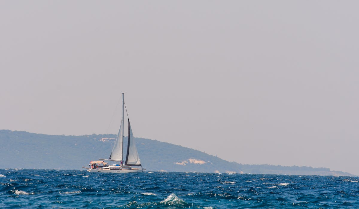 Sailboat on blue ocean with distant coastline visible