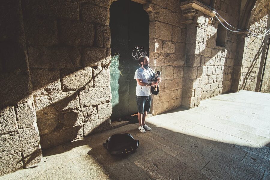 Street musician playing bagpipes beside a historic stone facade in Santiago de Compostela