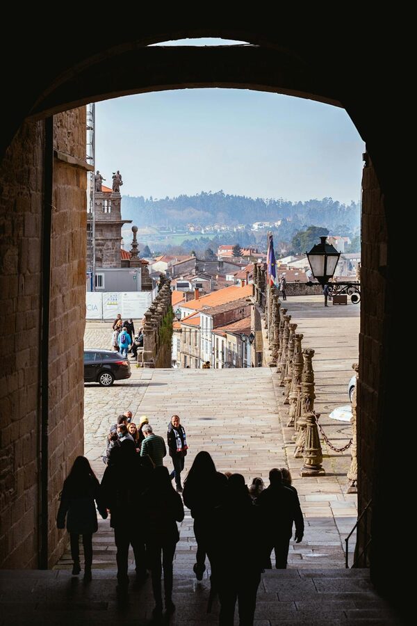 Silhouettes of visitors walking through a medieval archway in Santiago