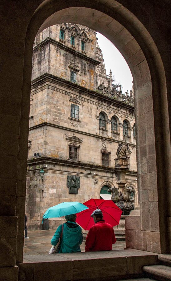 People with umbrellas walking through a historic archway in Santiago