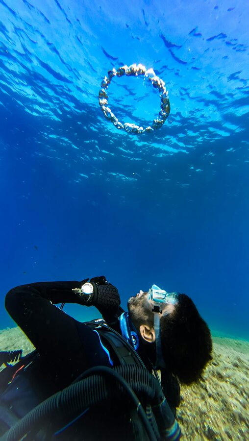 Scuba diver creating a bubble ring in clear blue waters during a dive