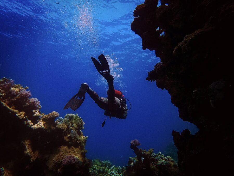Scuba diver navigating through coral formations in deep blue ocean water